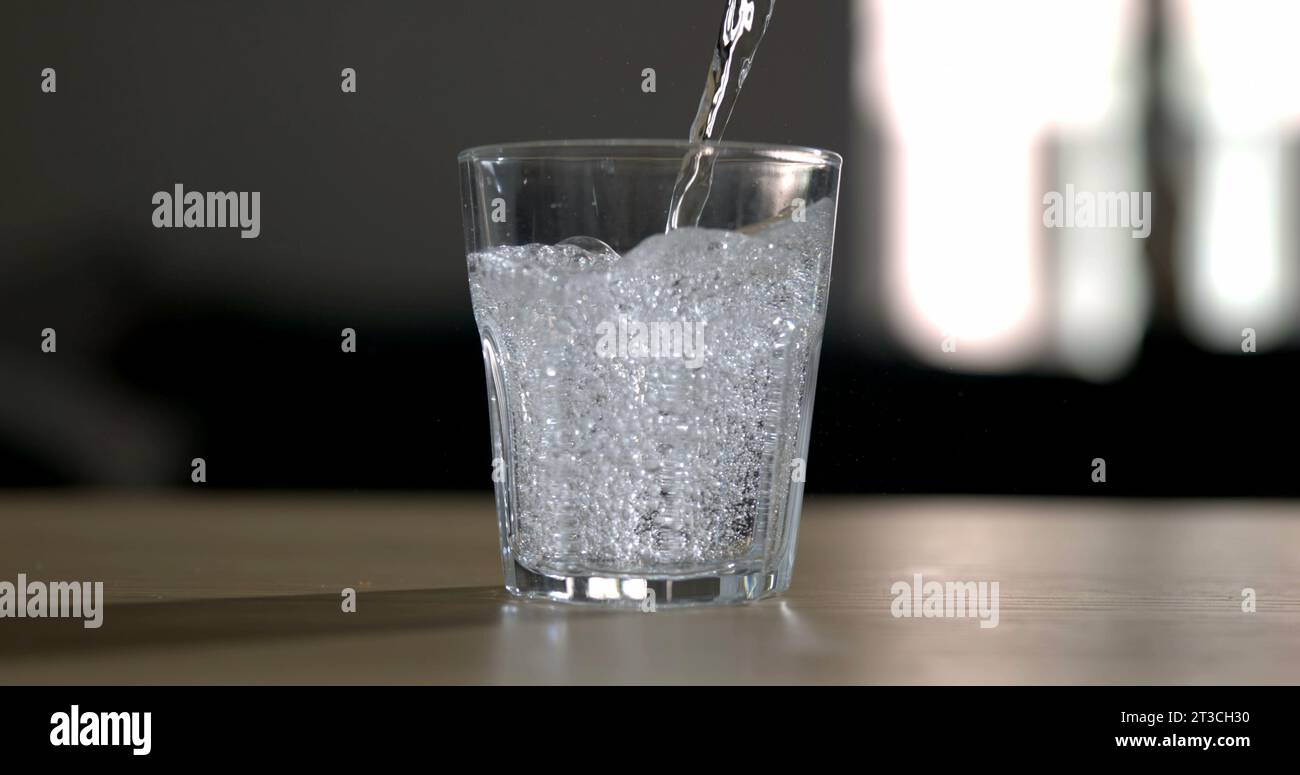 Pouring sprinkling water into glass cup in super slow-motion 800 fps. Serving hydrating drink ...