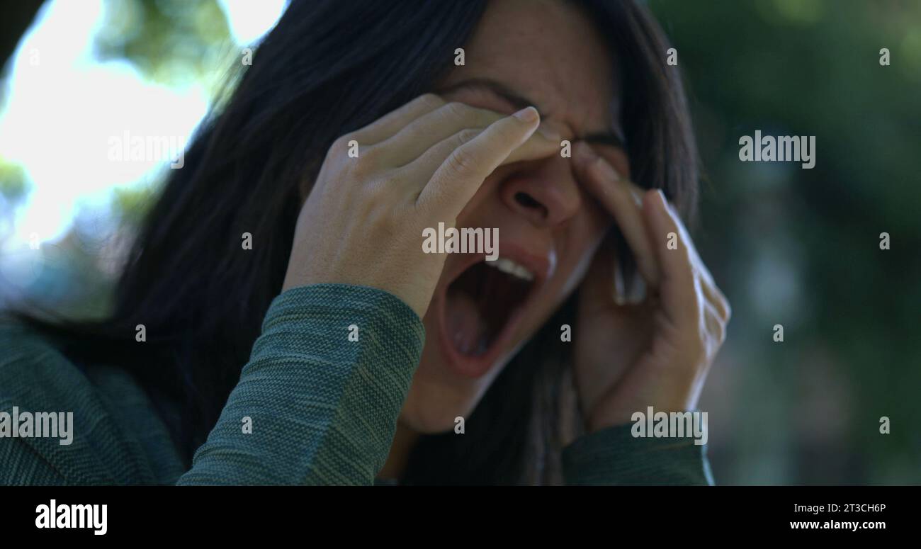 Tired woman yawning and rubbing eyes and face with hands standing ...