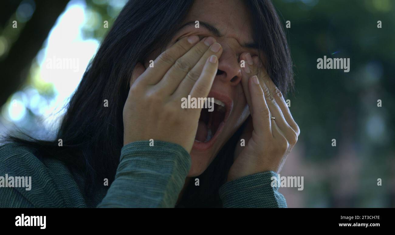 Tired woman yawning and rubbing eyes and face with hands standing ...