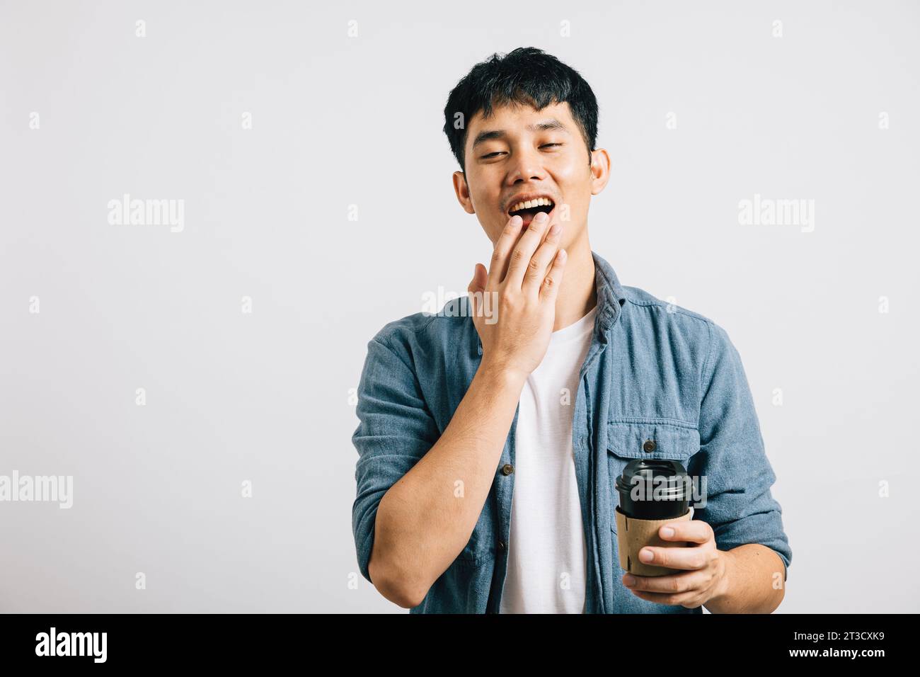 a tired and sad young man closes his eyes, yawning as he holds a take ...