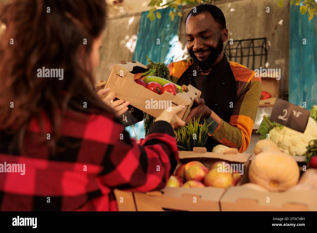 African american man showing box of natural farming produce to woman at ...