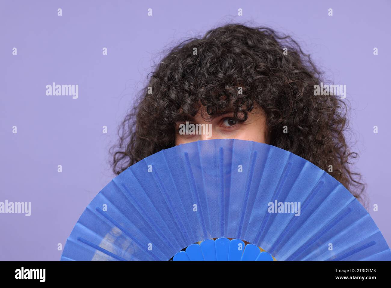 Woman hiding her face behind hand fan on purple background Stock Photo ...