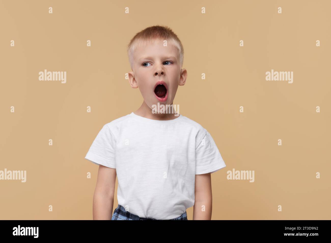 Sleepy boy yawning on beige background. Insomnia problem Stock Photo ...
