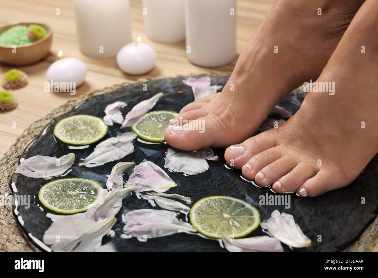 Woman soaking her feet in plate with water, flower petals and lime ...