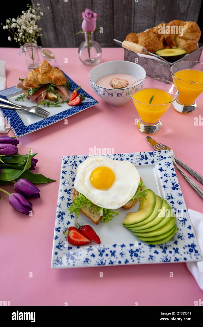 Brunch for two people with a beautiful pink background, Croissants, avocadoes, orange juice ...