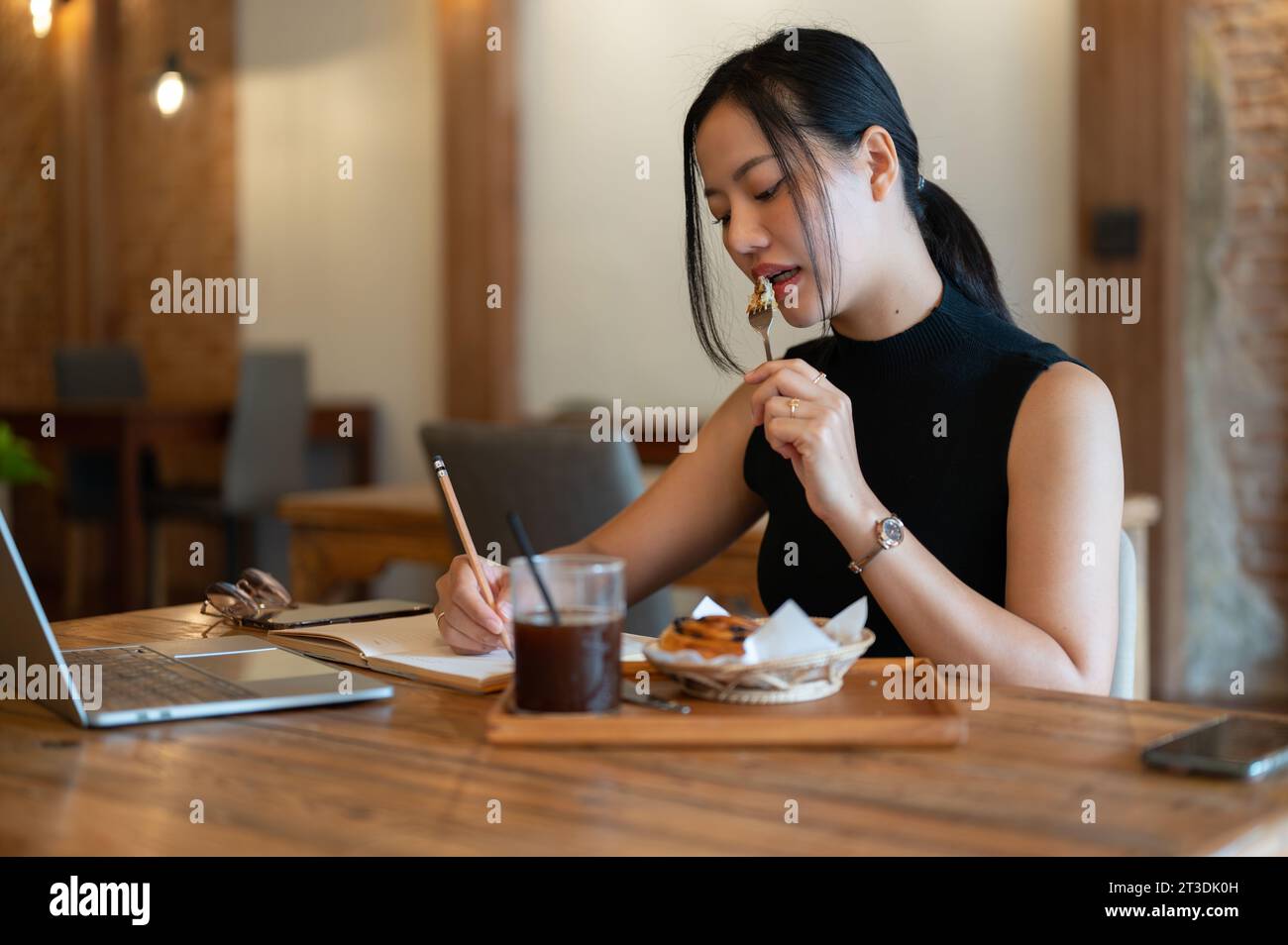 A gorgeous millennial Asian woman is having breakfast while working ...