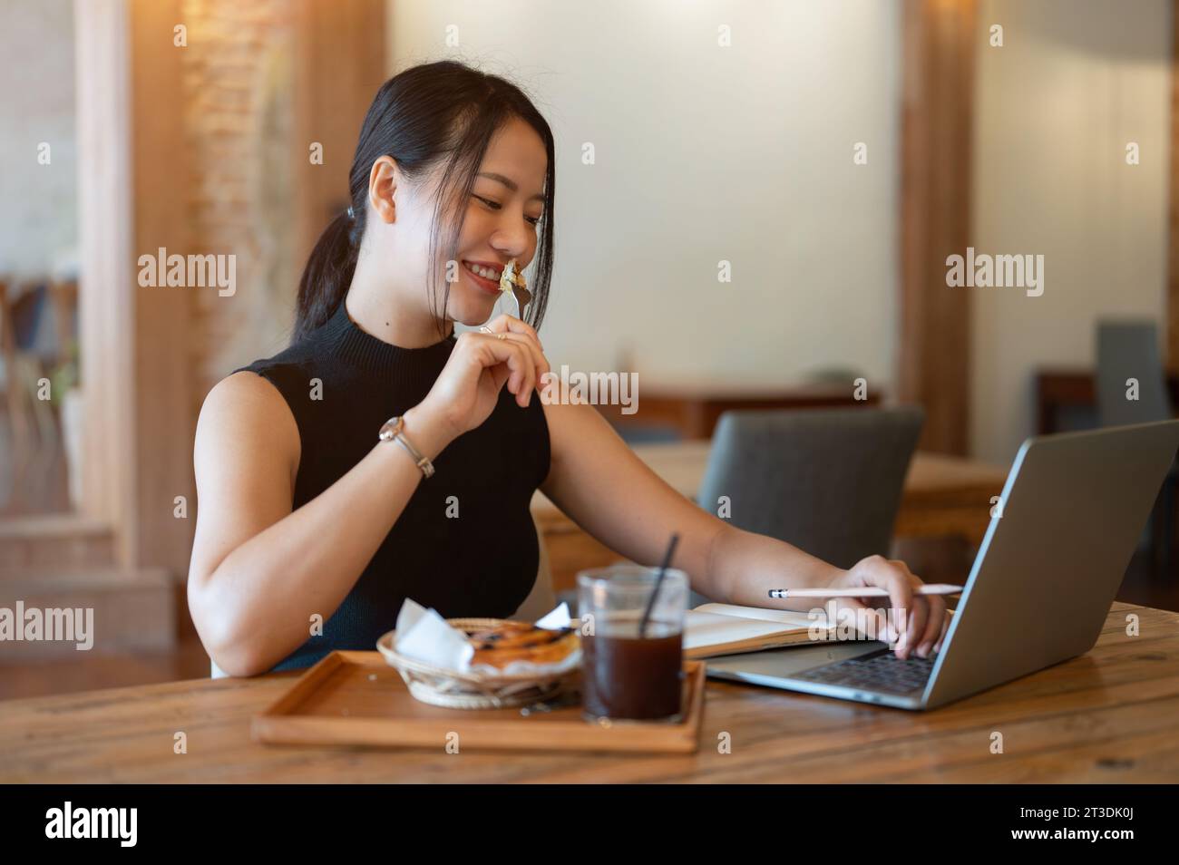 A gorgeous millennial Asian woman is having breakfast while working ...