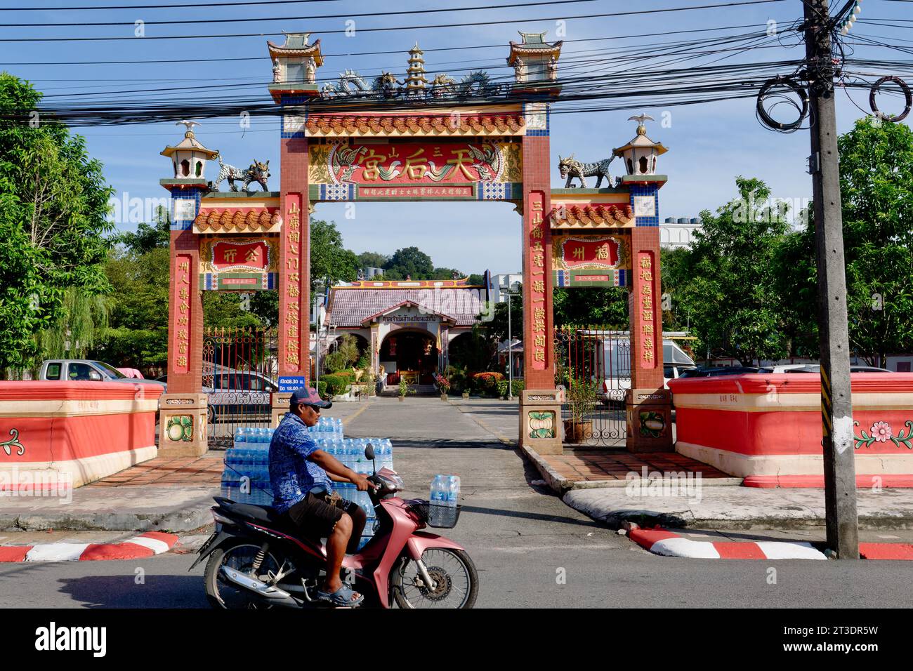 A motorcycle delivery man rides past Sam San Tian Huo Geung Shrine (Wat ...