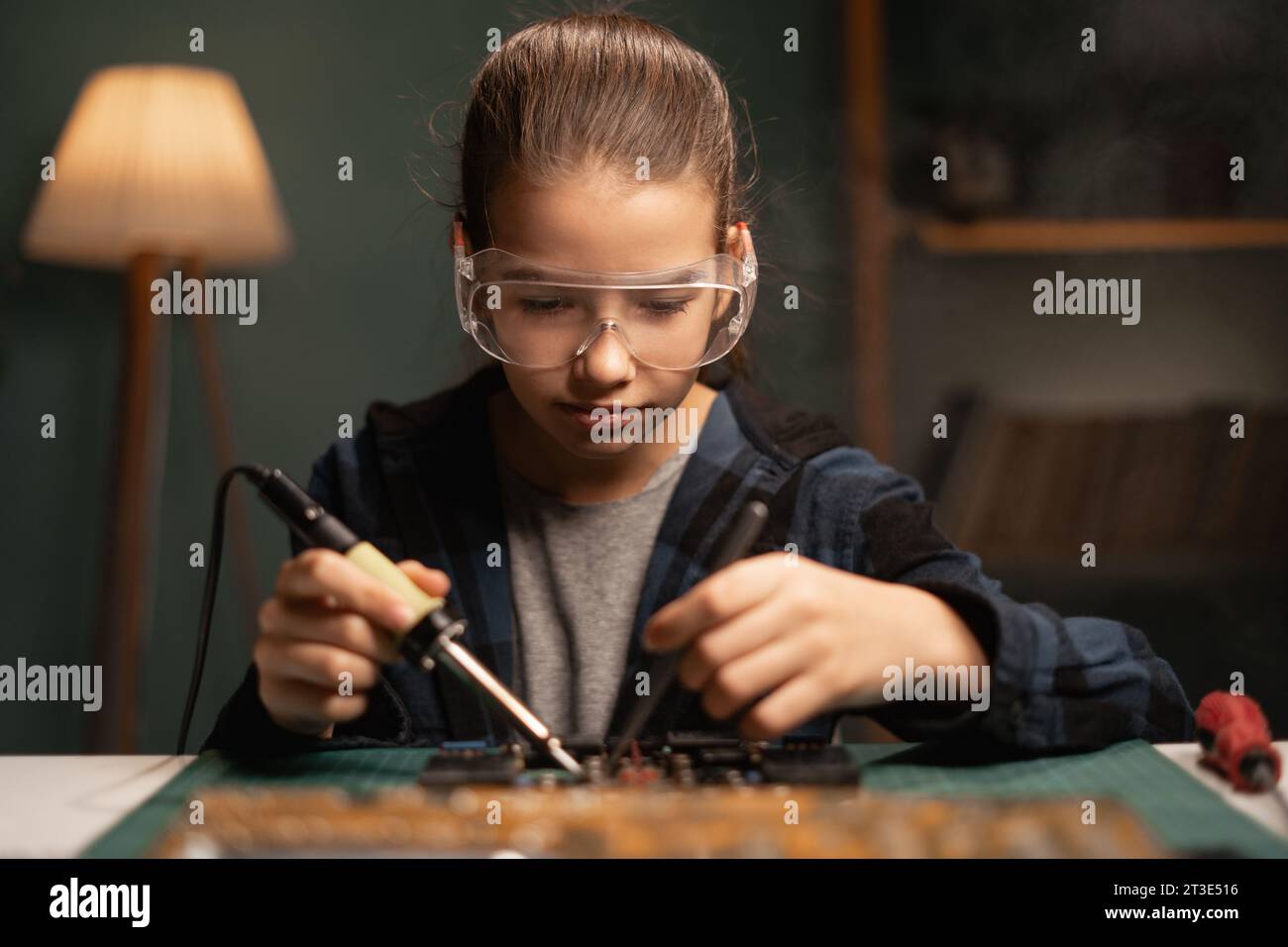 Smart teenage girl is studying electronics and soldering circuit boards ...