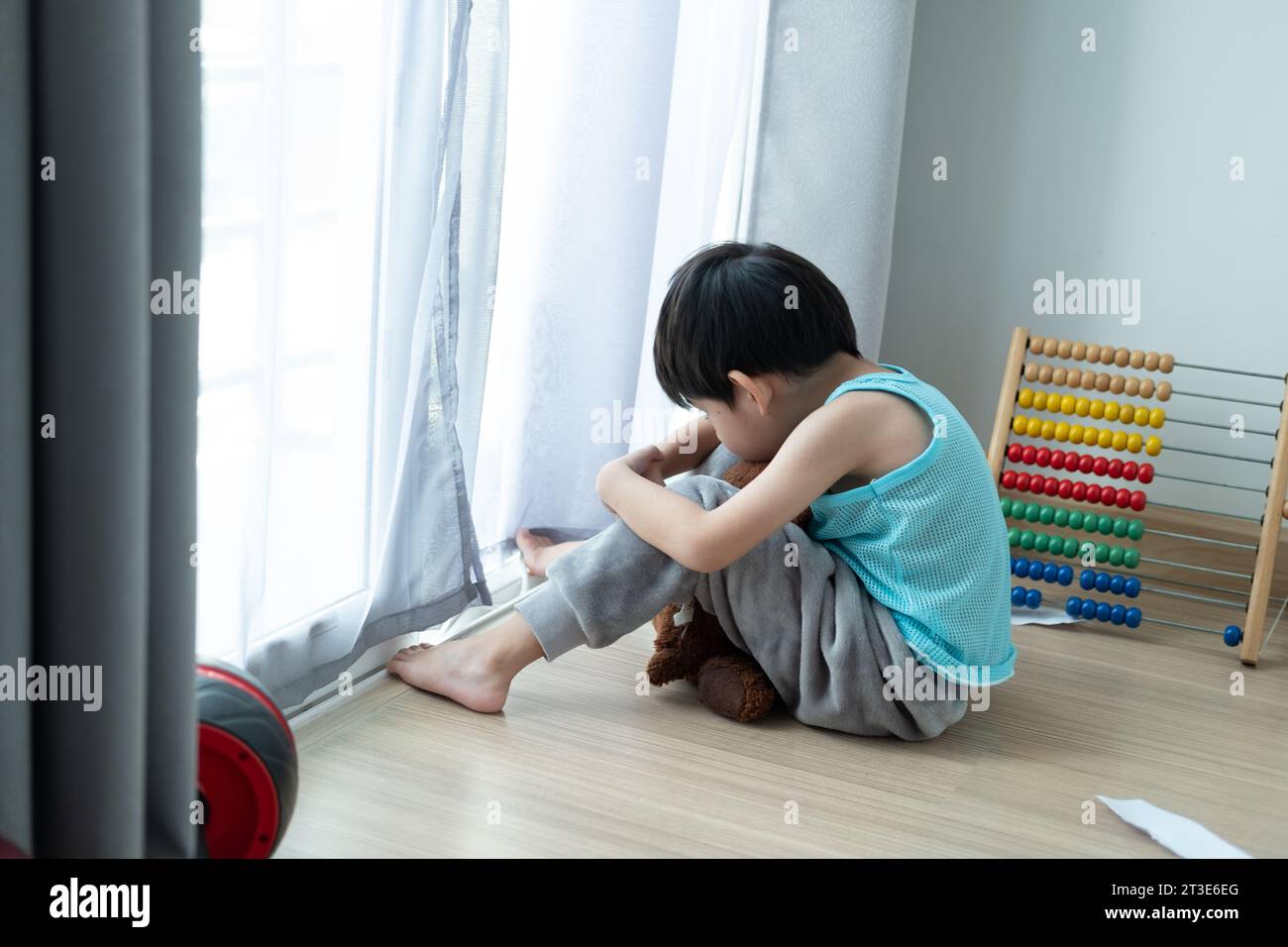 Sad Asian boy sits with his head down and looks out the door at his ...