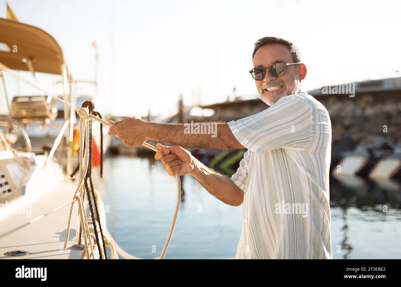 Senior man confidently manages rope, docking his yacht at marina Stock ...