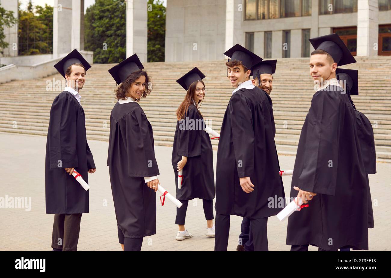 Graduate students standing in university campus in black robes with ...