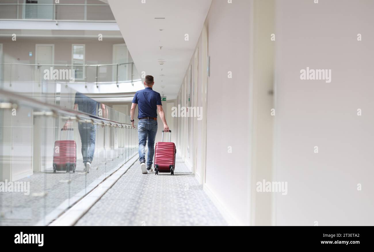 Man with suitcase walking down in hotel corridor back view Stock Photo ...