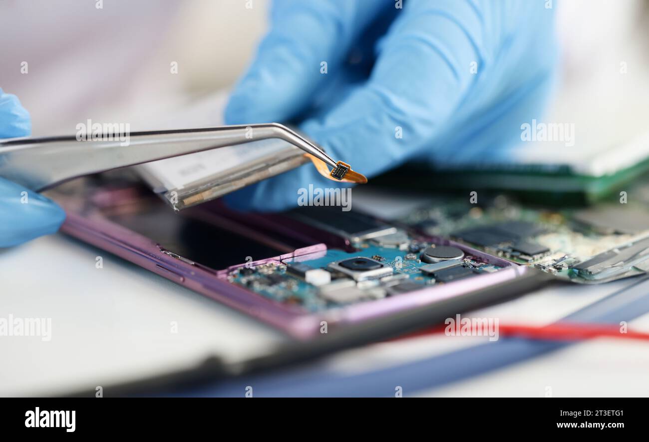 Master in rubber gloves holding microchip over broken phone in workshop ...