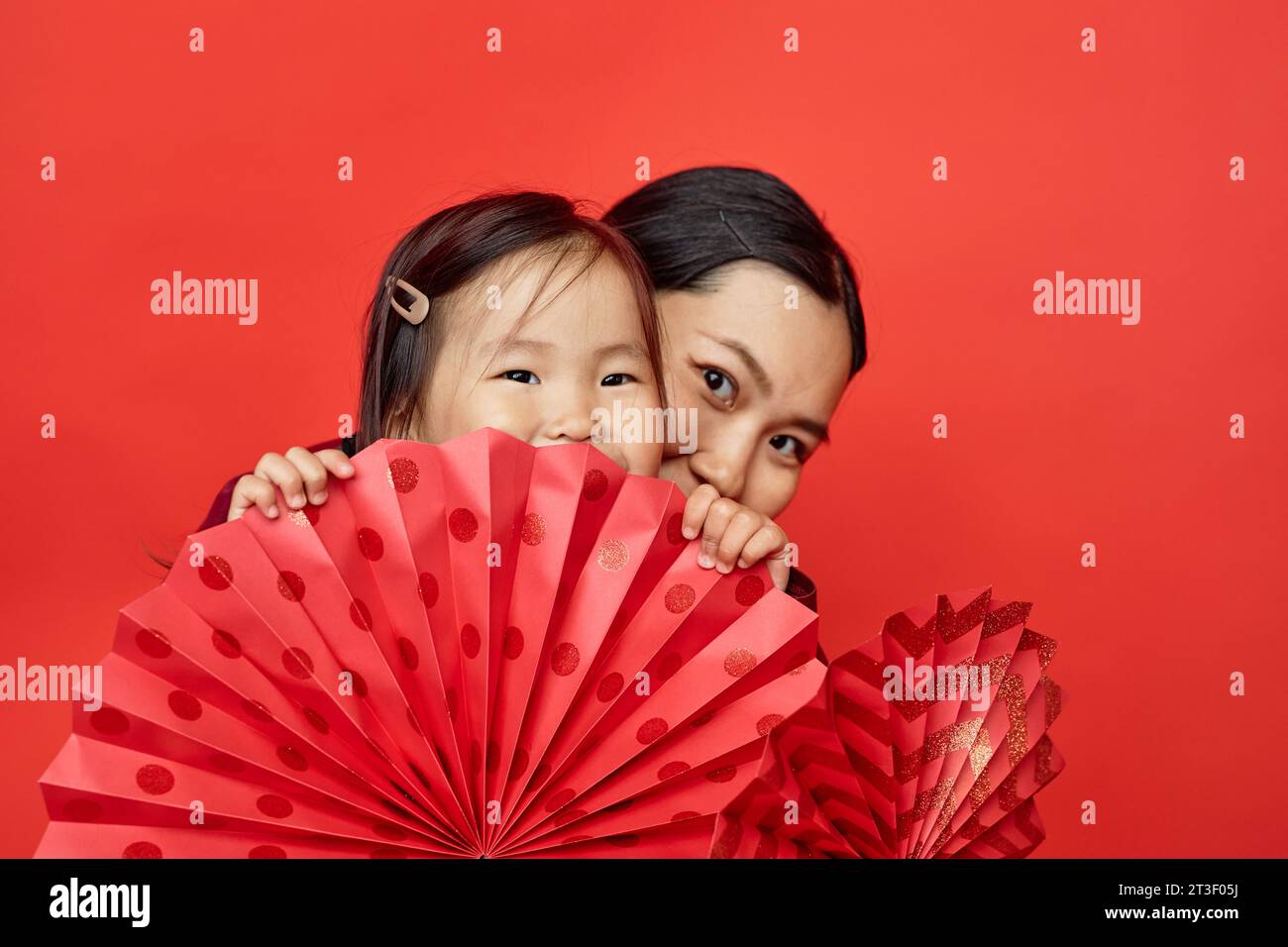 Portrait of playful Asian mother with little girl holding paper fans ...