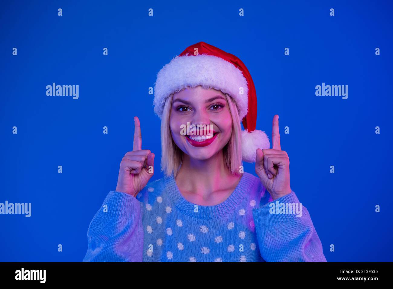 Photo of sweet shiny lady santa helper dressed ugly print xmas sweater pointing two fingers up ...