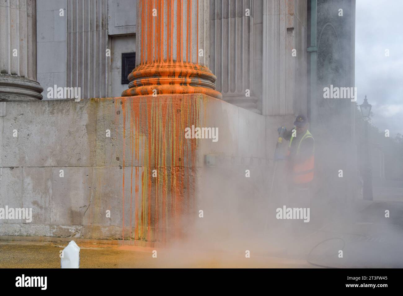 London, UK. 25th October 2023. A worker cleans the orange paint sprayed ...