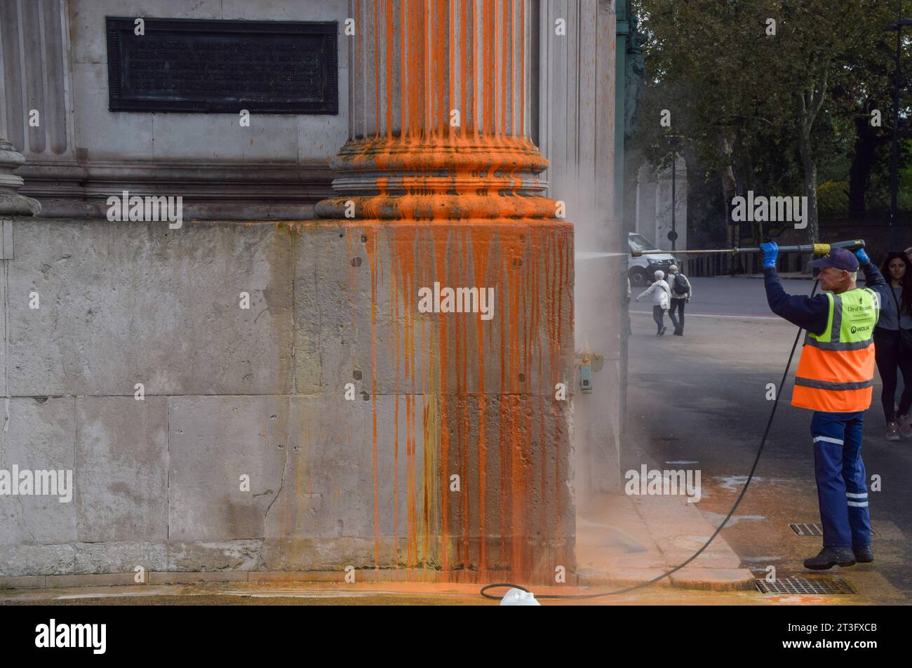 London, UK. 25th October 2023. A worker cleans the orange paint sprayed ...
