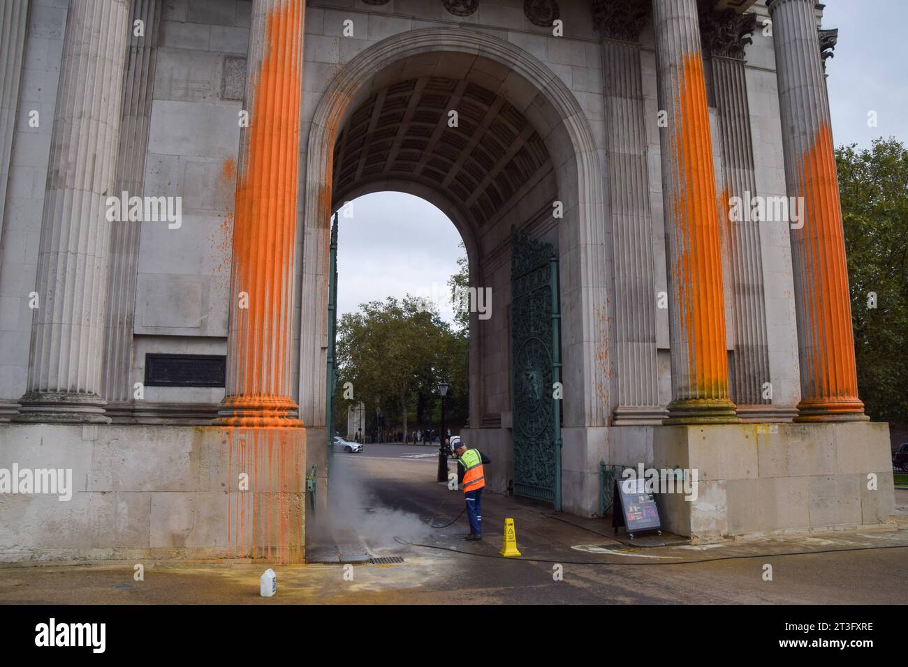 London, UK. 25th October 2023. A worker cleans the orange paint sprayed ...