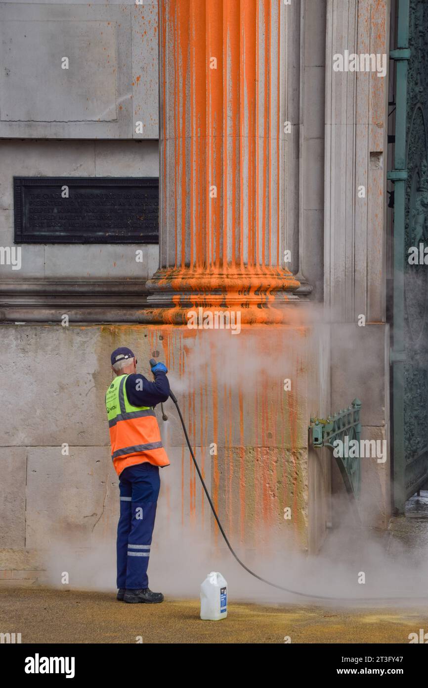 London, UK. 25th October 2023. A worker cleans the orange paint sprayed ...