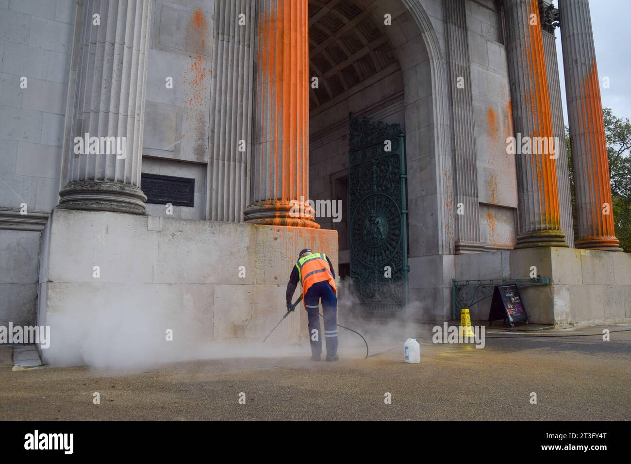 London, UK. 25th October 2023. A worker cleans the orange paint sprayed ...