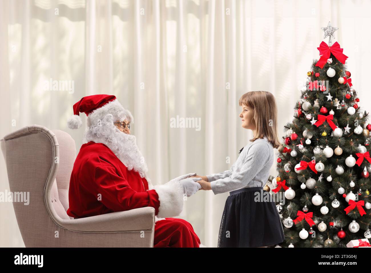 Santa claus seated in an armchair and holding hands with a girl at home ...