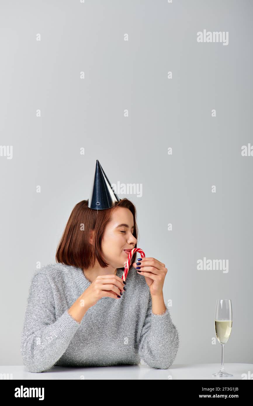 happy woman in party cap kissing candy cane near champagne glass on ...