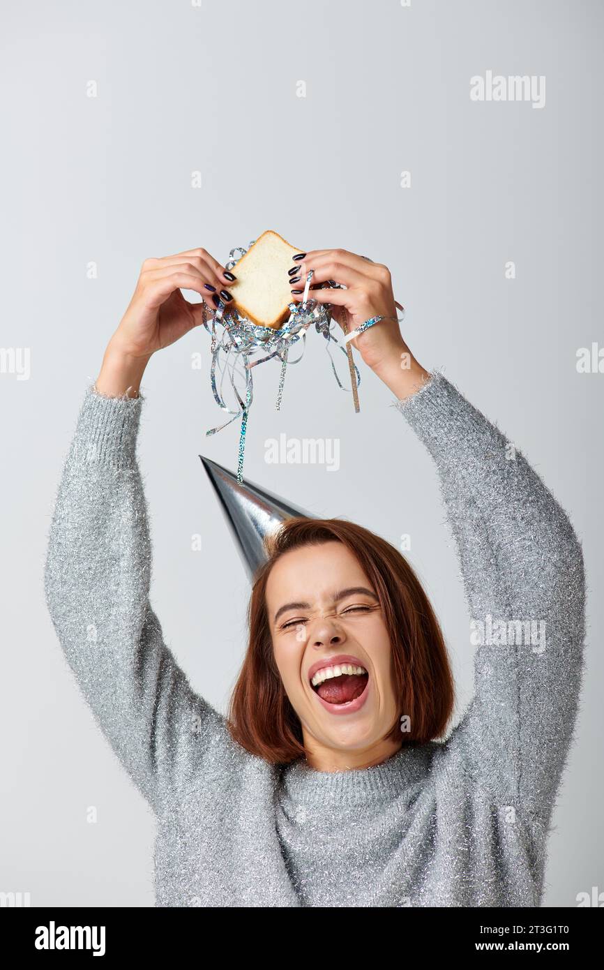 excited woman in party cap holding sandwich with tinsel above head on ...