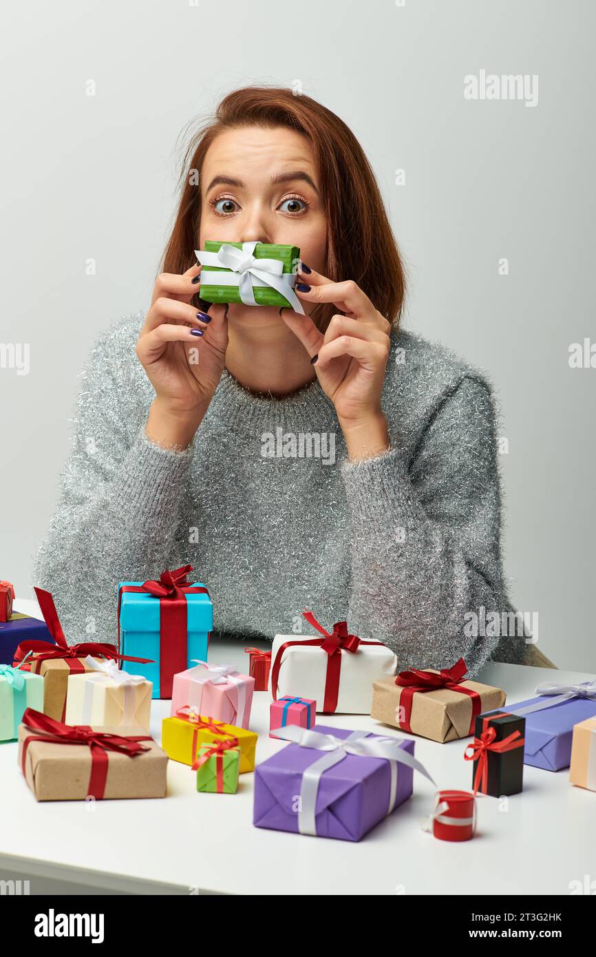 funny woman in sweater holding tiny Christmas present near face and ...