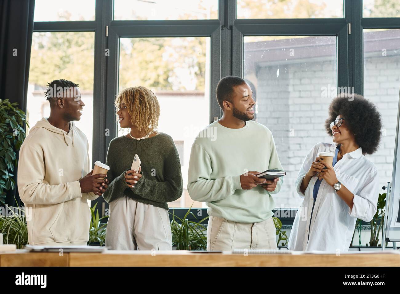 four team members smiling at each other holding coffee cups, plants on ...