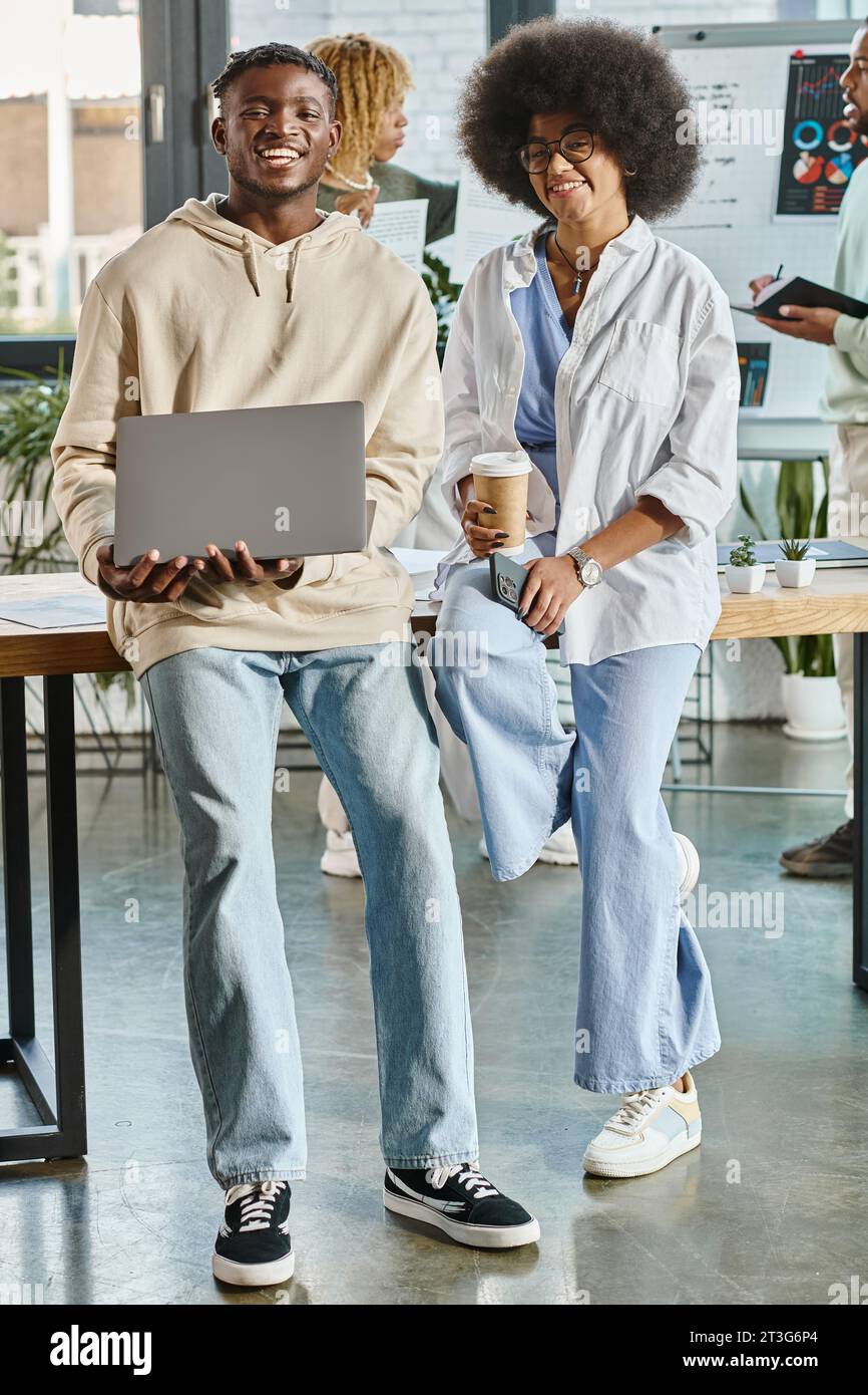 cheerful colleagues looking at camera holding laptop with their friend ...