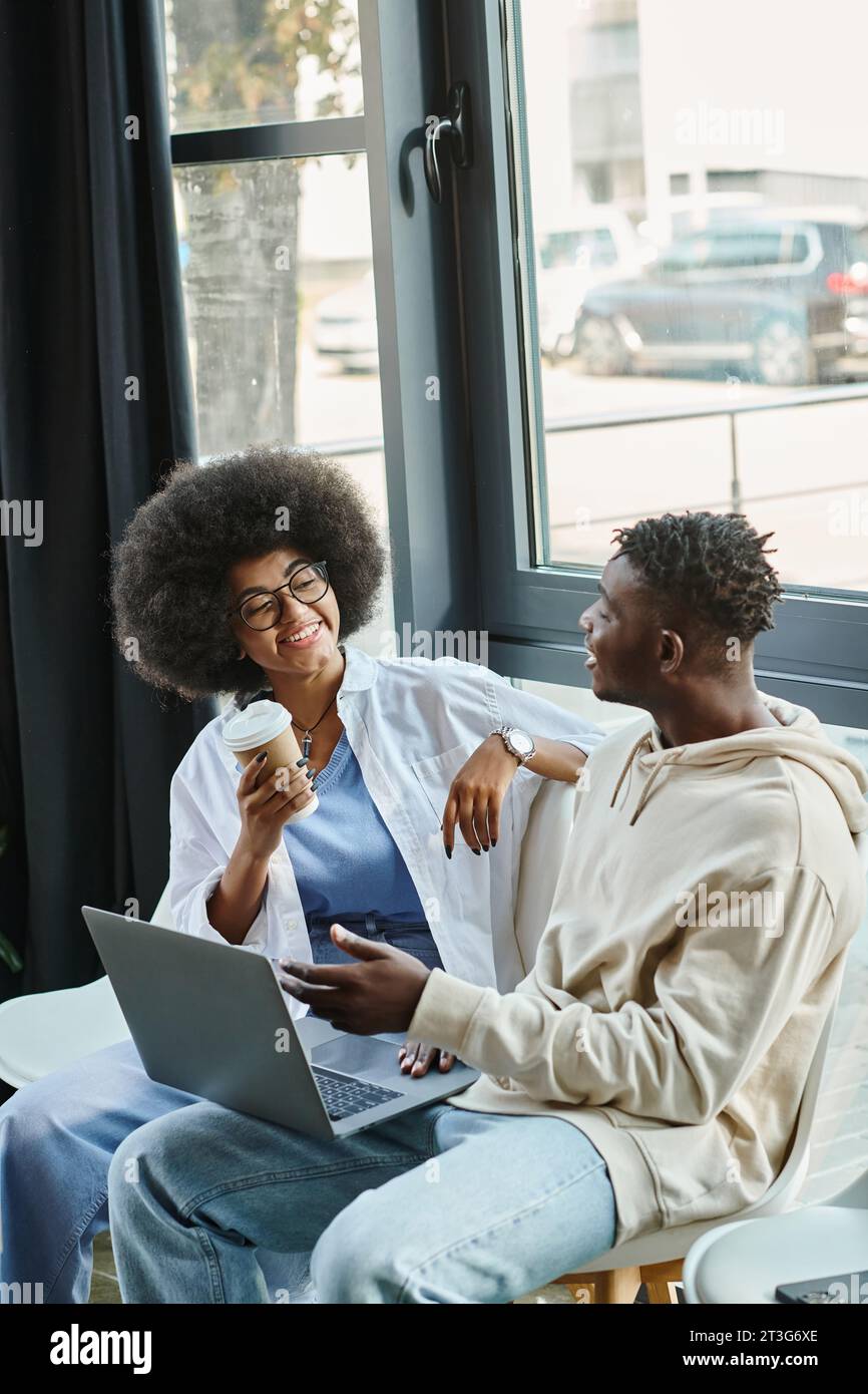joyful friends in casual outfits with coffee cup and laptop smiling at ...