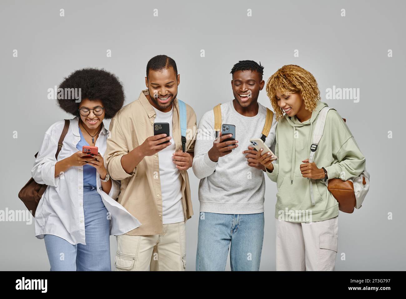 cheerful young friends in urban street wear looking at their phones and ...