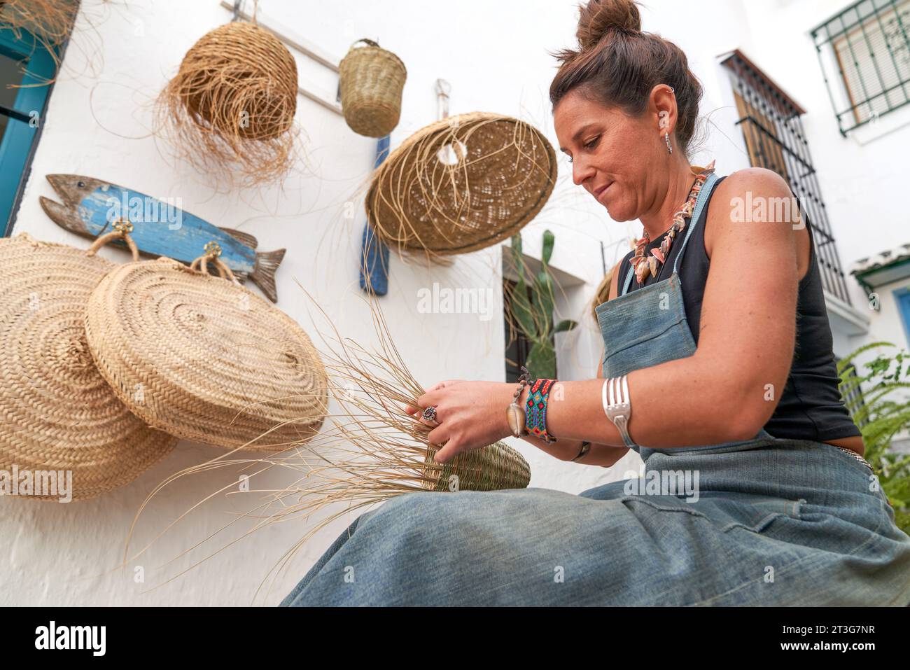 Side view of Hispanic woman weaving a basket with esparto fibers ...