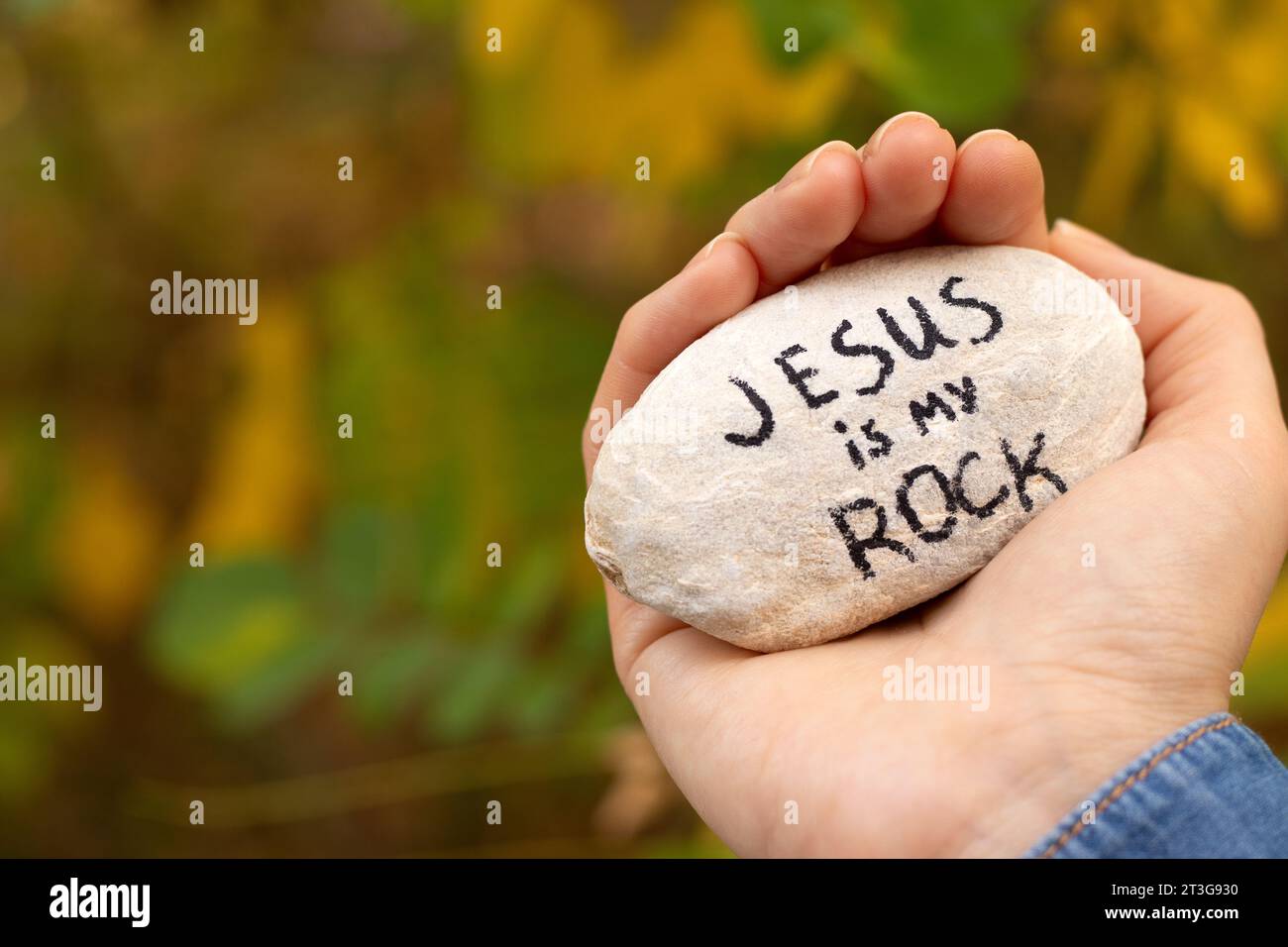 Hand holding a stone with handwriting "Jesus is My Rock" in nature ...