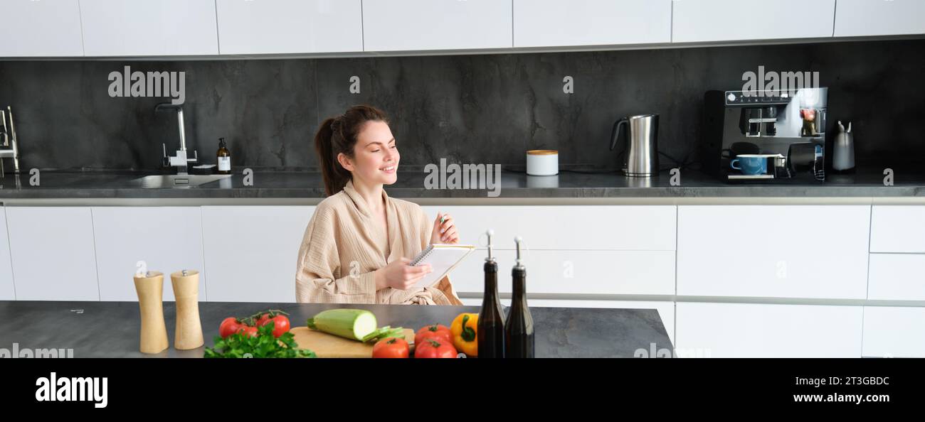 Portrait of woman thinking of menu, sitting in the kitchen and making ...