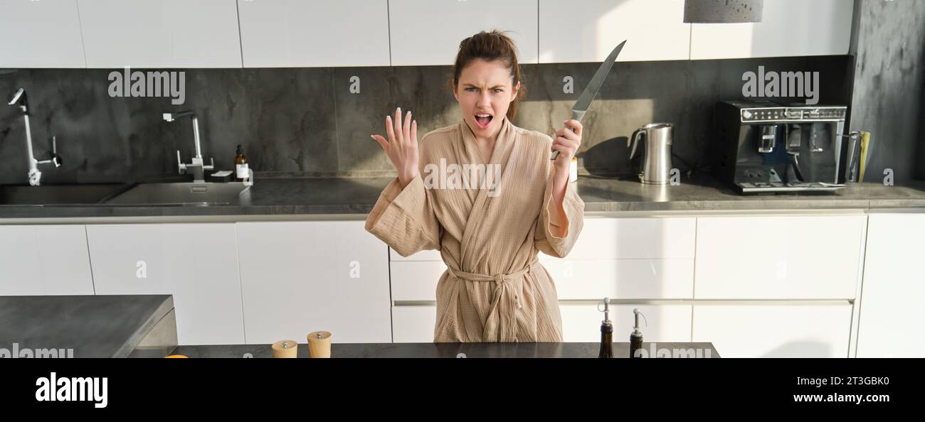 Portrait of annoyed woman with knife, angry while cooking in the ...