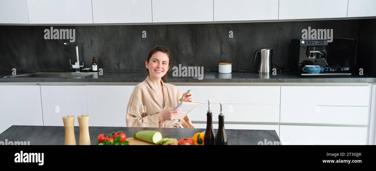Portrait of woman thinking of menu, sitting in the kitchen and making ...