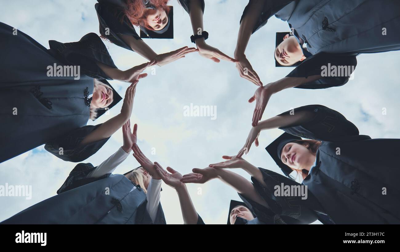 Graduate students in black robes and caps make a circle shape from ...