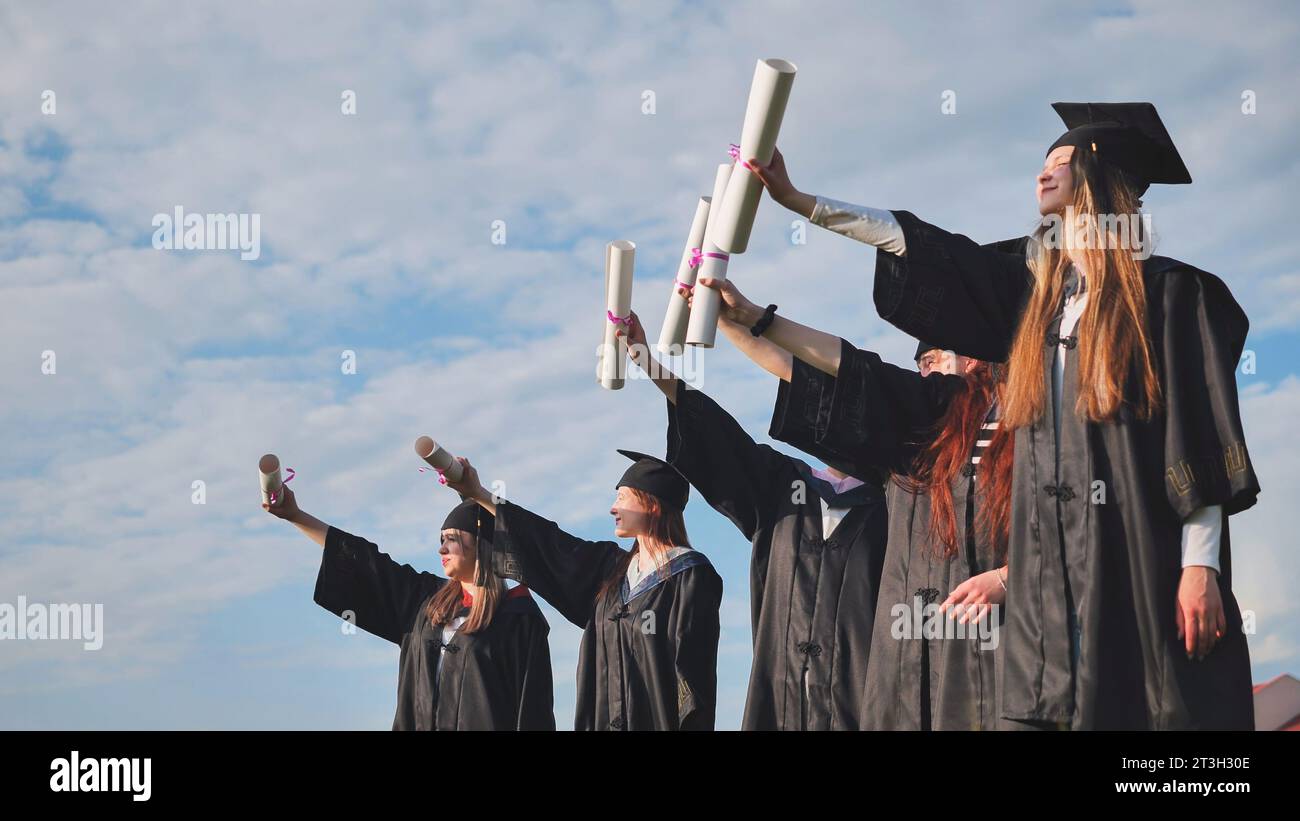Cheerful graduates pose with raised diplomas on a sunny day Stock Photo ...
