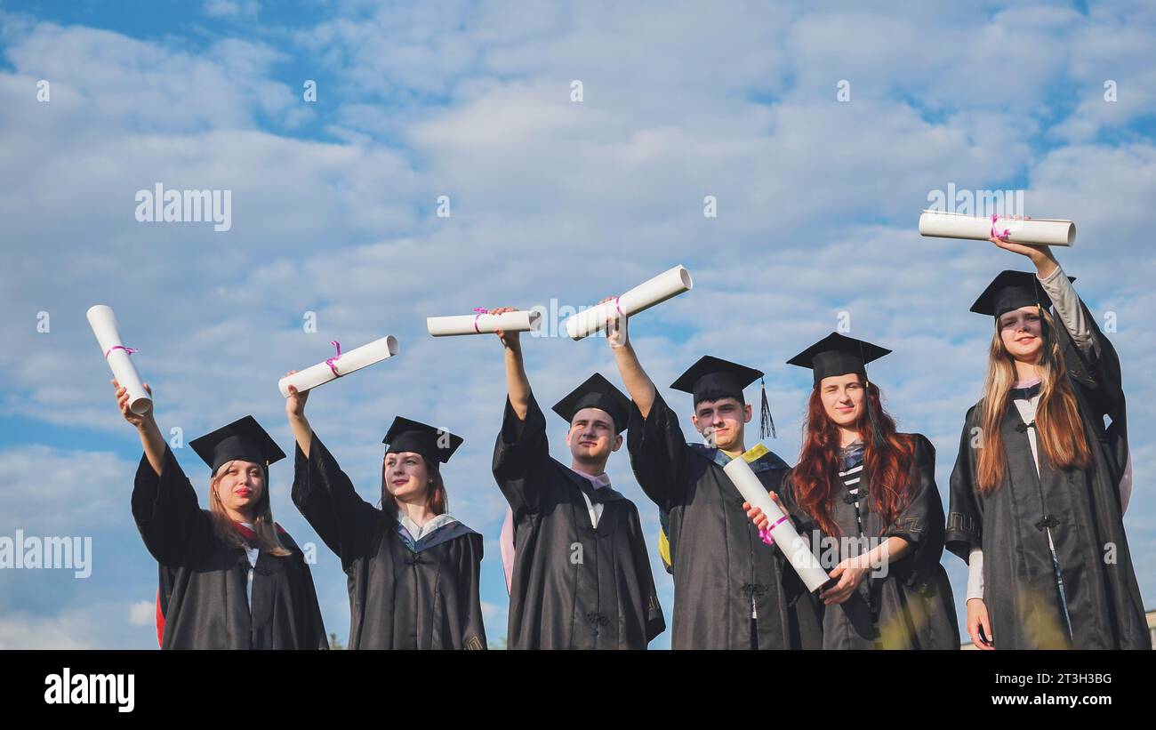 Cheerful graduates pose with raised diplomas on a sunny day Stock Photo ...
