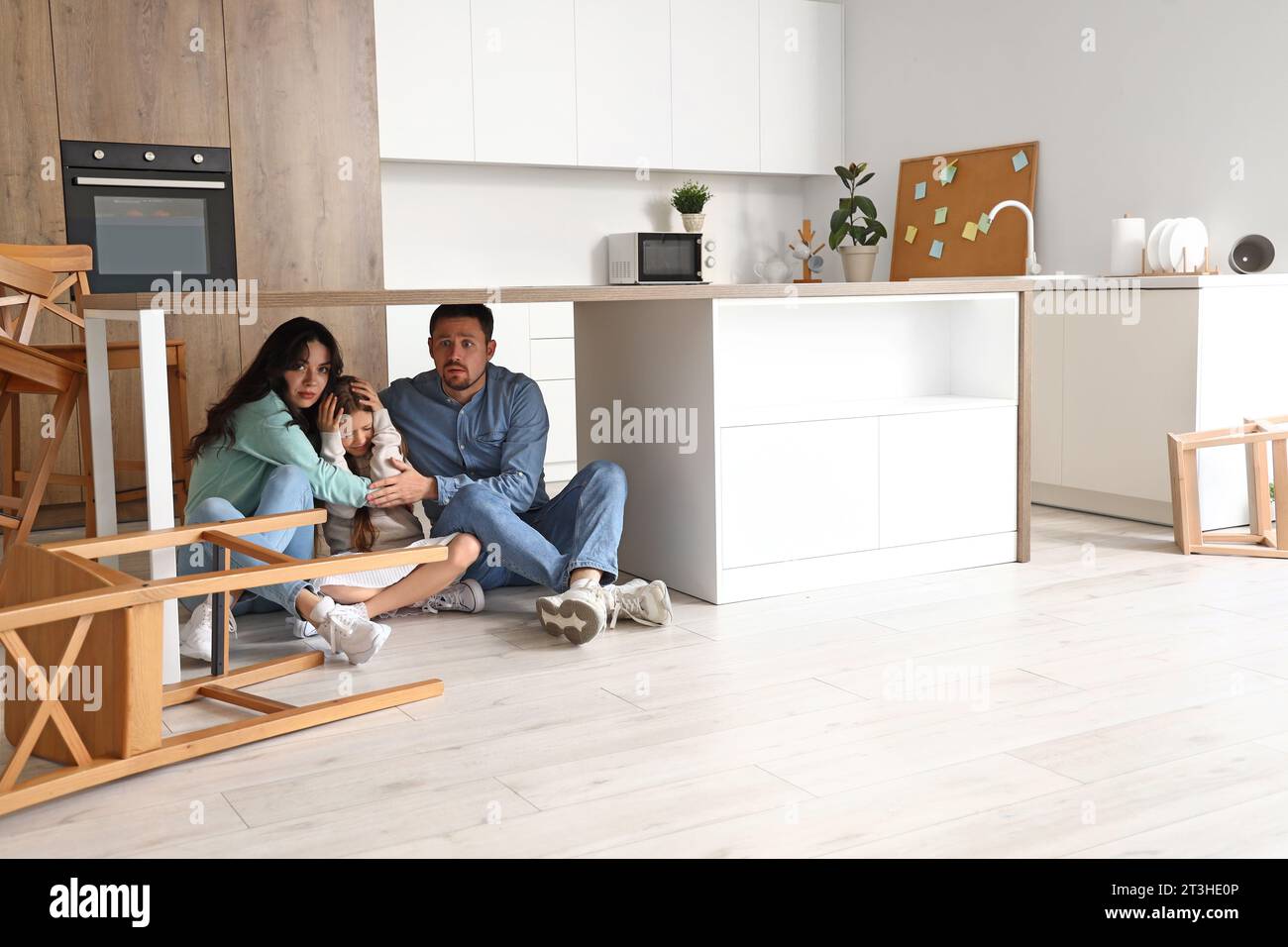 Scared family hiding under dining table during earthquake in kitchen ...