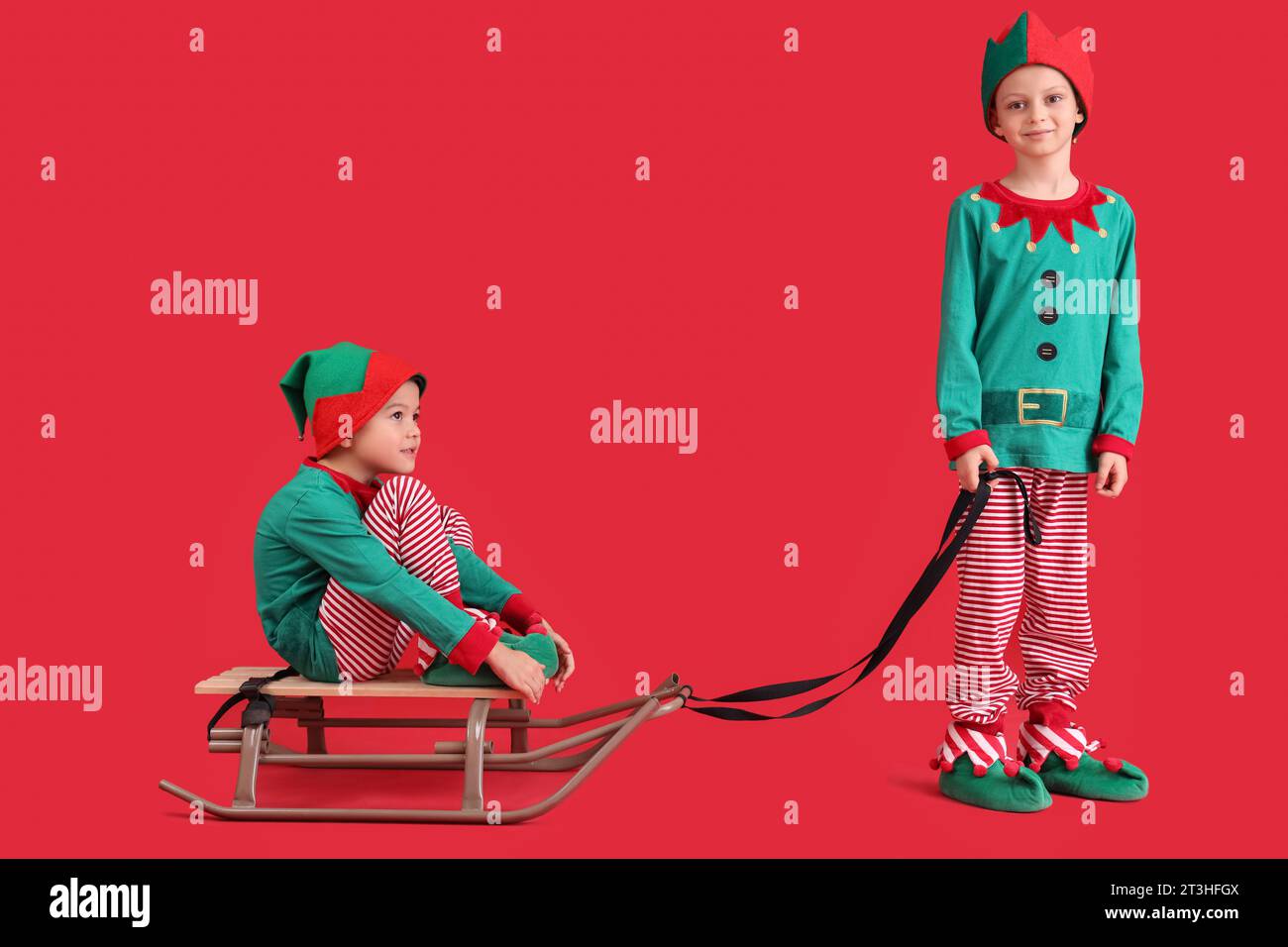 Cute little boys in elf costumes with sledge on red background Stock ...