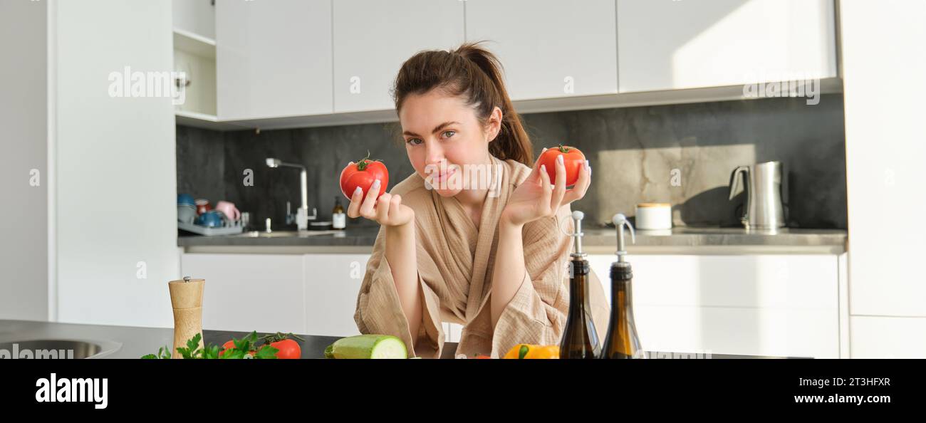 Portrait of woman cooking at home in the kitchen, holding tomatoes ...