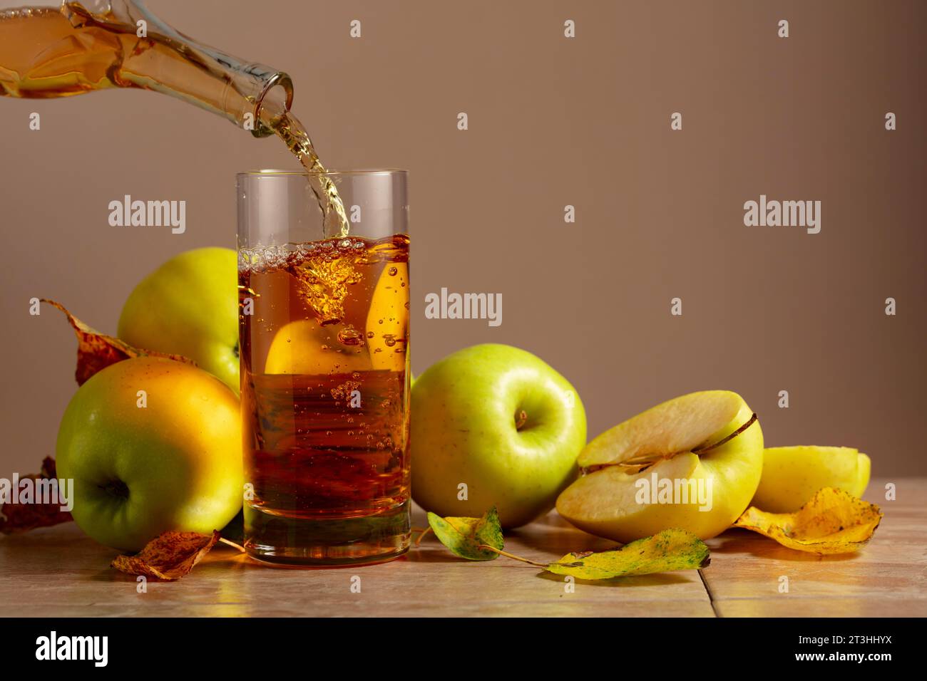 Apple juice is poured from a bottle into a glass. On a ceramic table ...