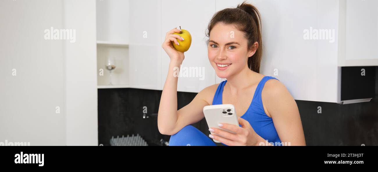 Portrait of fitness woman, sitting in kitchen with smartphone ...
