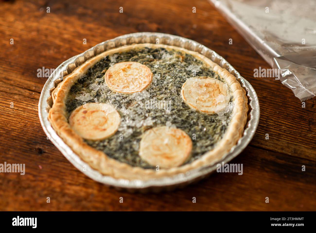 A round, frozen quiche with cheese and spinach displayed against a ...
