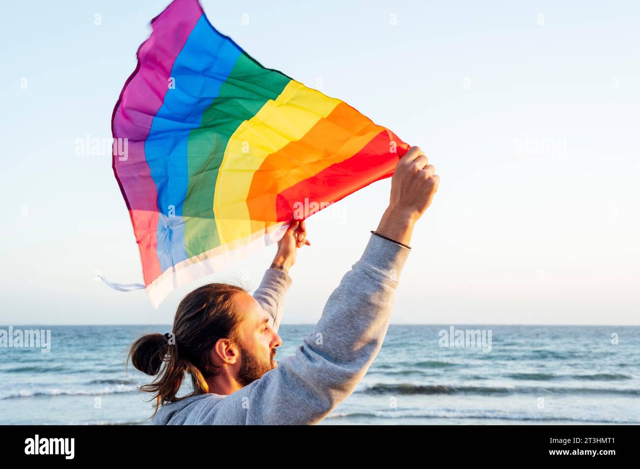 silhouette of a man holding a gay pride rainbow flag blowing in the ...
