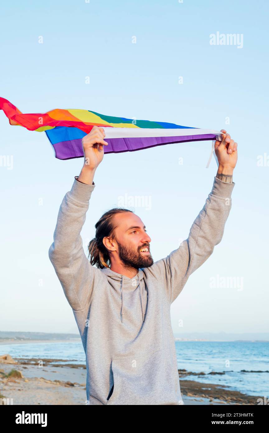 Cheerful boy with a lgbtq rainbow flag on the beach. Young man holding ...