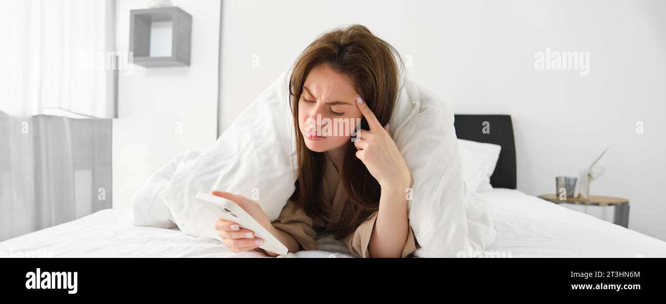 Woman with confused face, waking up in morning and checking her mobile ...